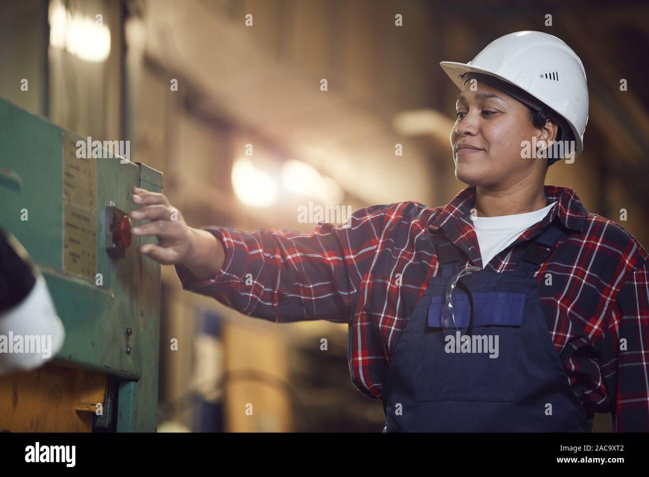 Waist up portrait of smiling female worker pushing red button while ...