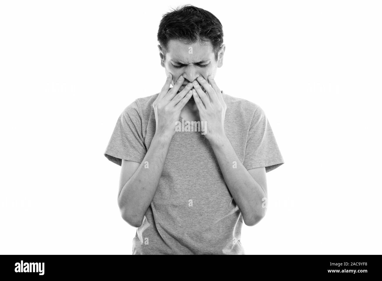 Studio shot of stressed young man looking tired while covering face ...