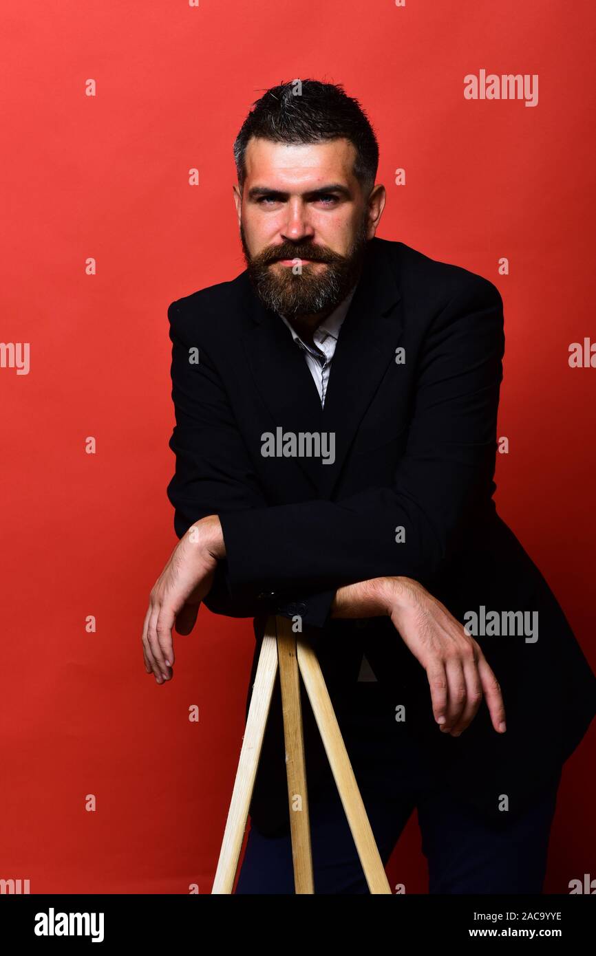 Macho man leans on photo tripod on red background. Man with beard ...