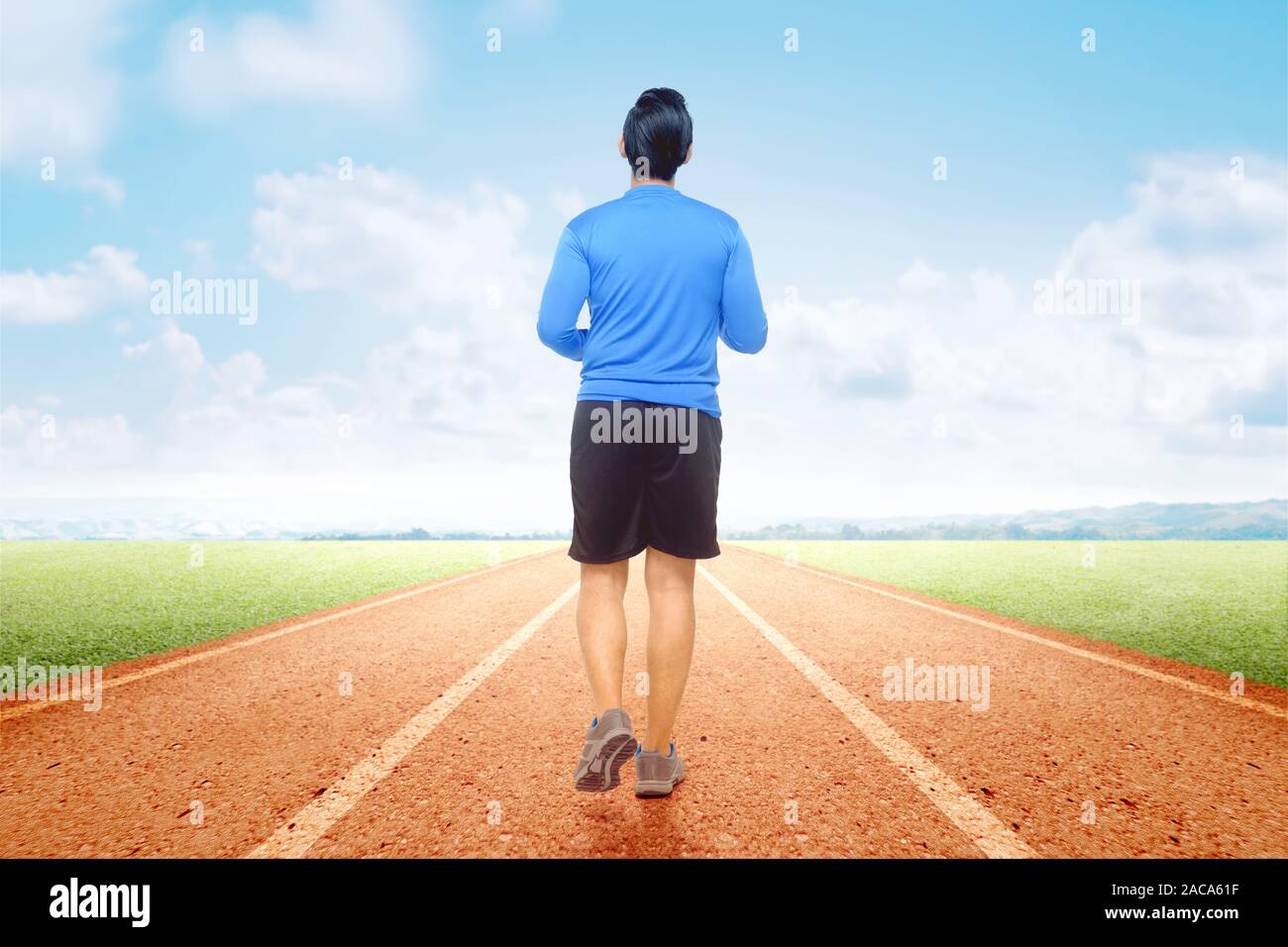 Rear view of Asian runner man running on the running track with a blue ...