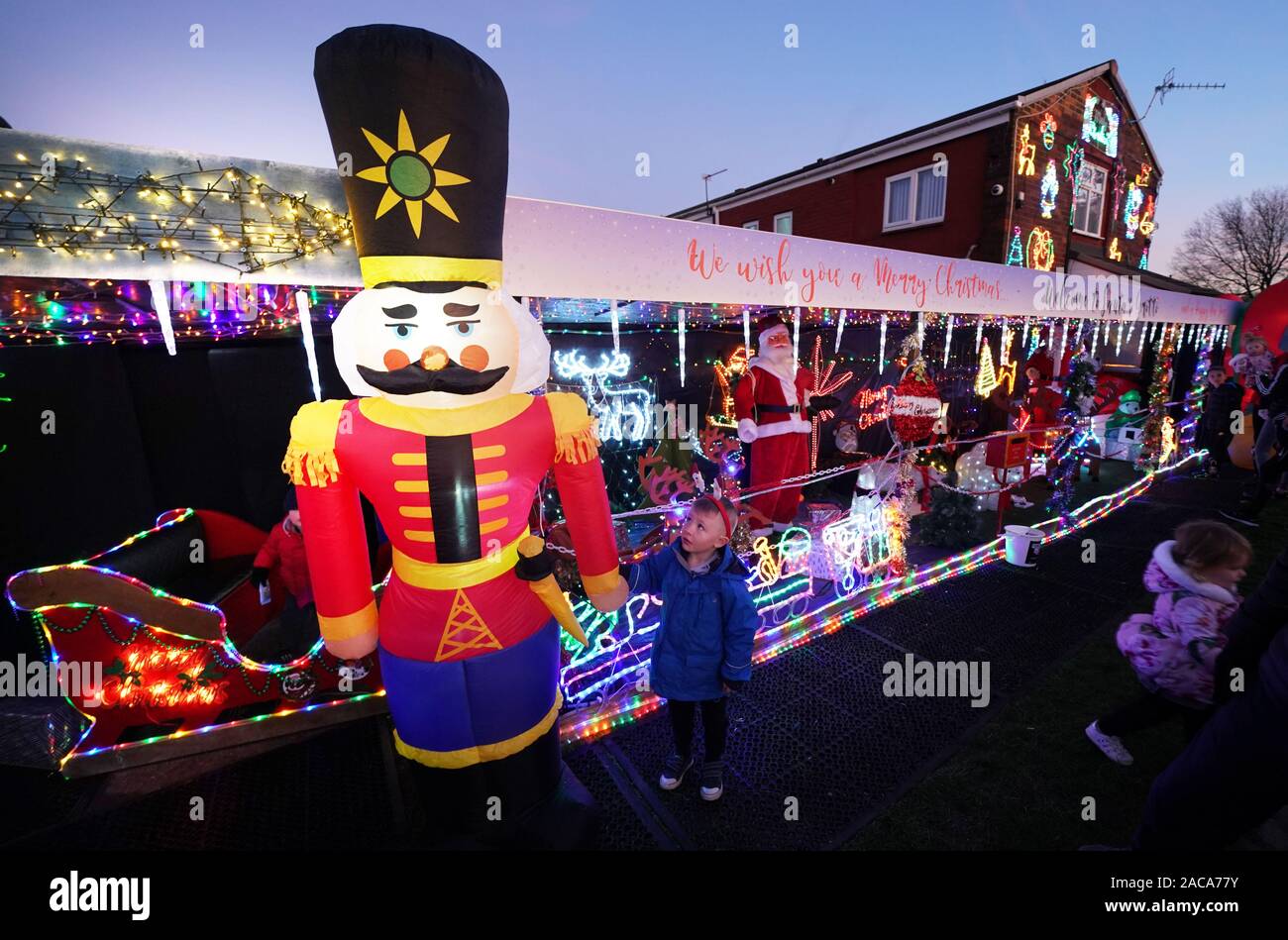 A young boy stands outside a house decorated with Christmas lights ...