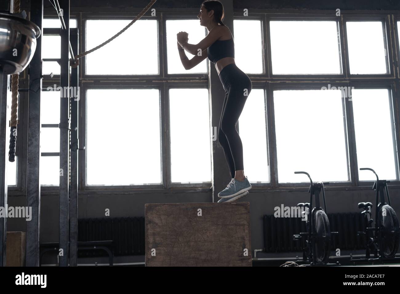Fit young woman box jumping at a crossfit style gym. Female athlete is ...