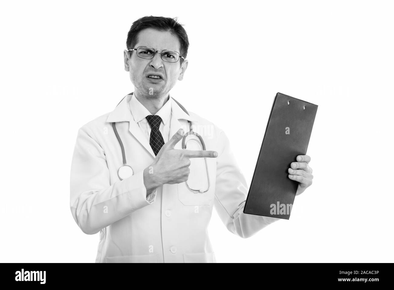 Studio shot of angry young man doctor holding and pointing at clipboard ...