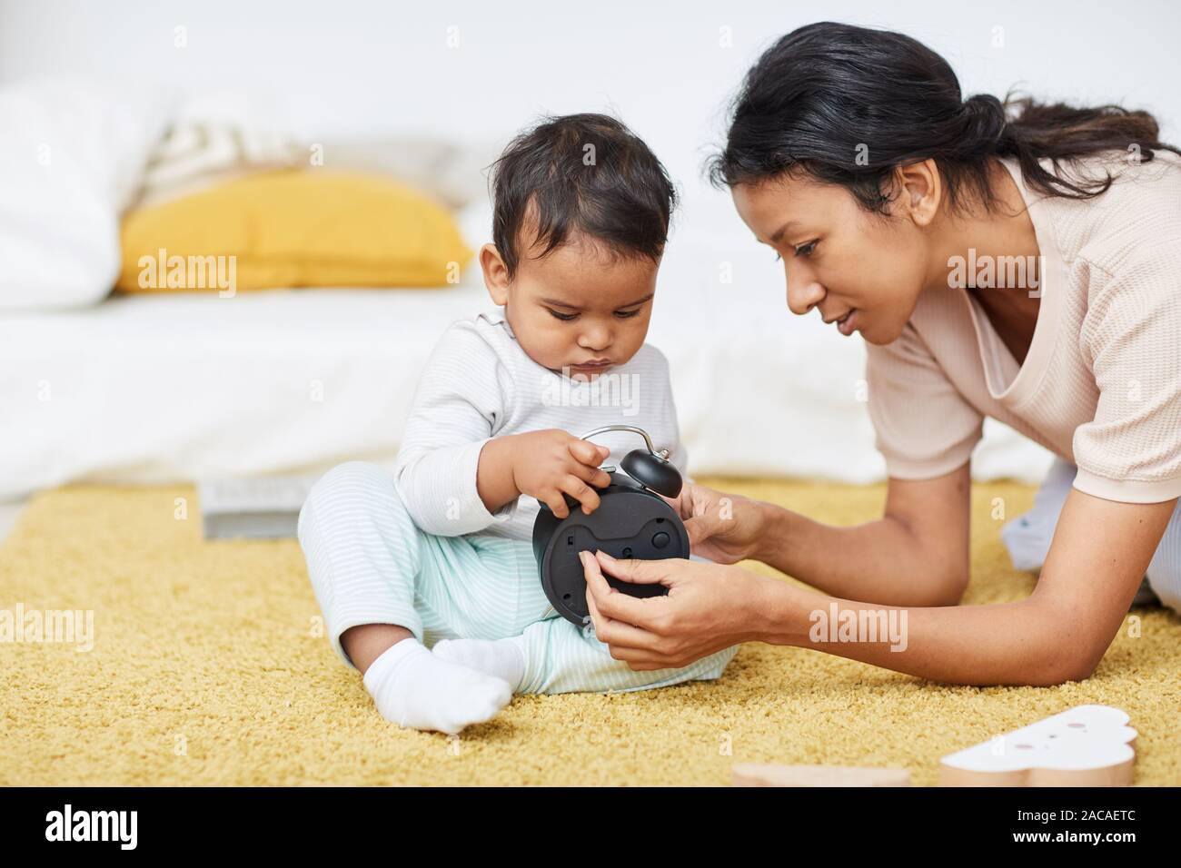 Young mother showing the alarm clock to her child and teaching him ...