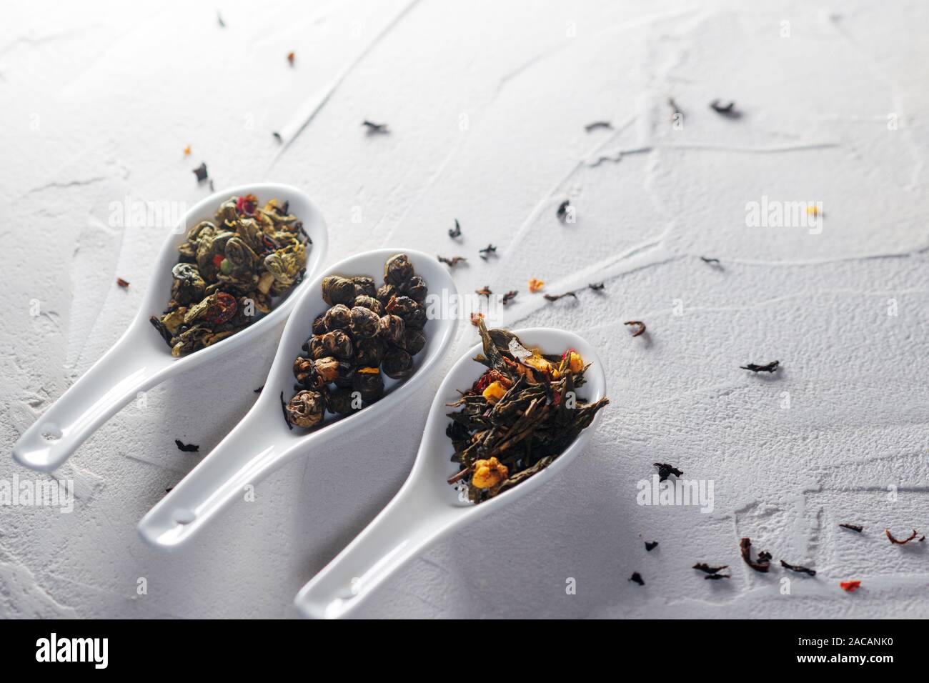Different varieties of tea leaves in white measuring spoons on a white ...