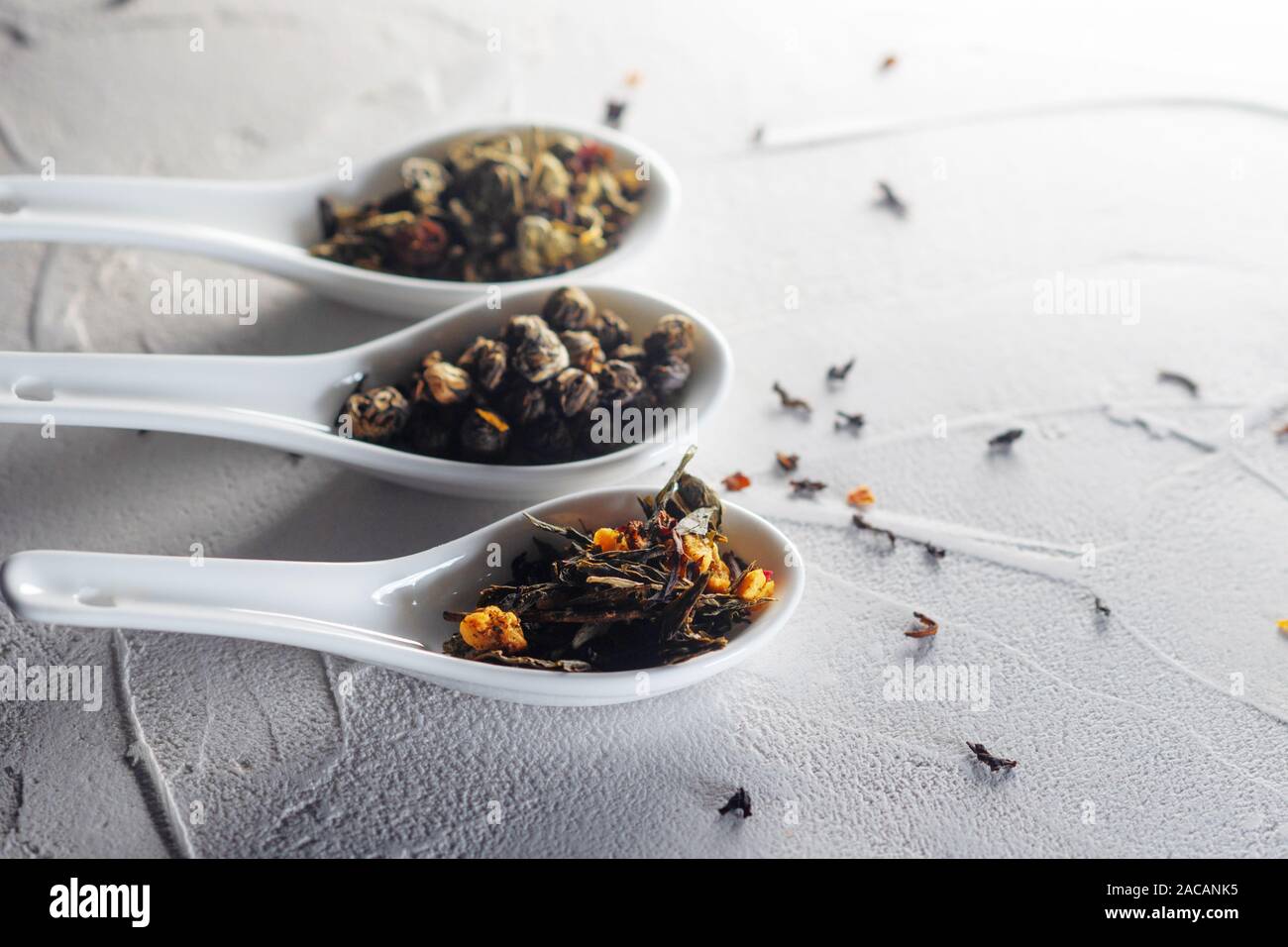 Different varieties of tea leaves in white measuring spoons on a white ...