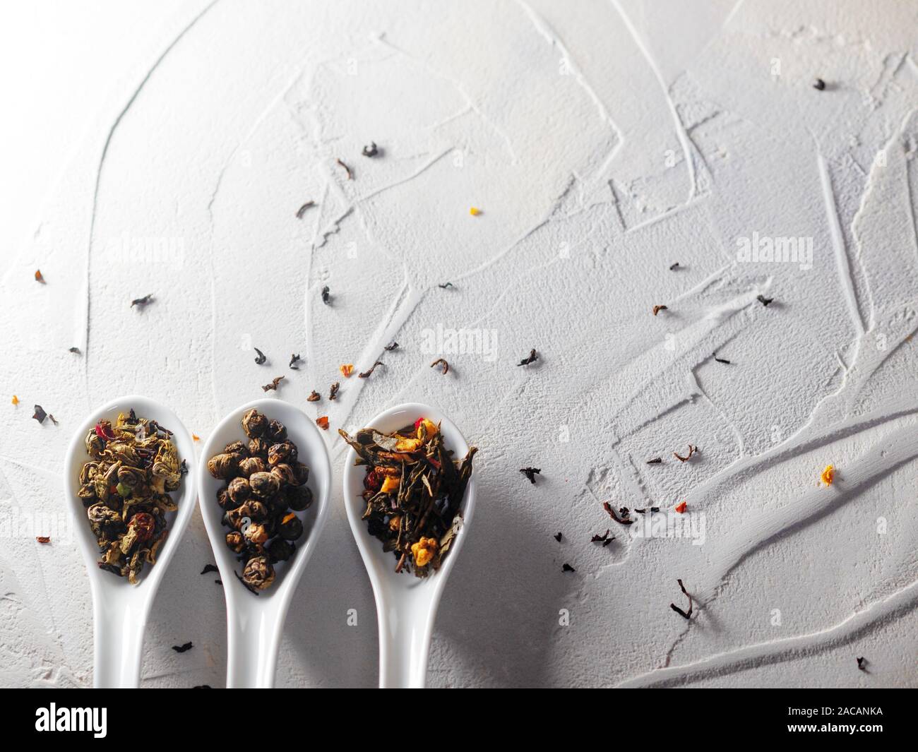 Different varieties of tea leaves in white measuring spoons on a white ...