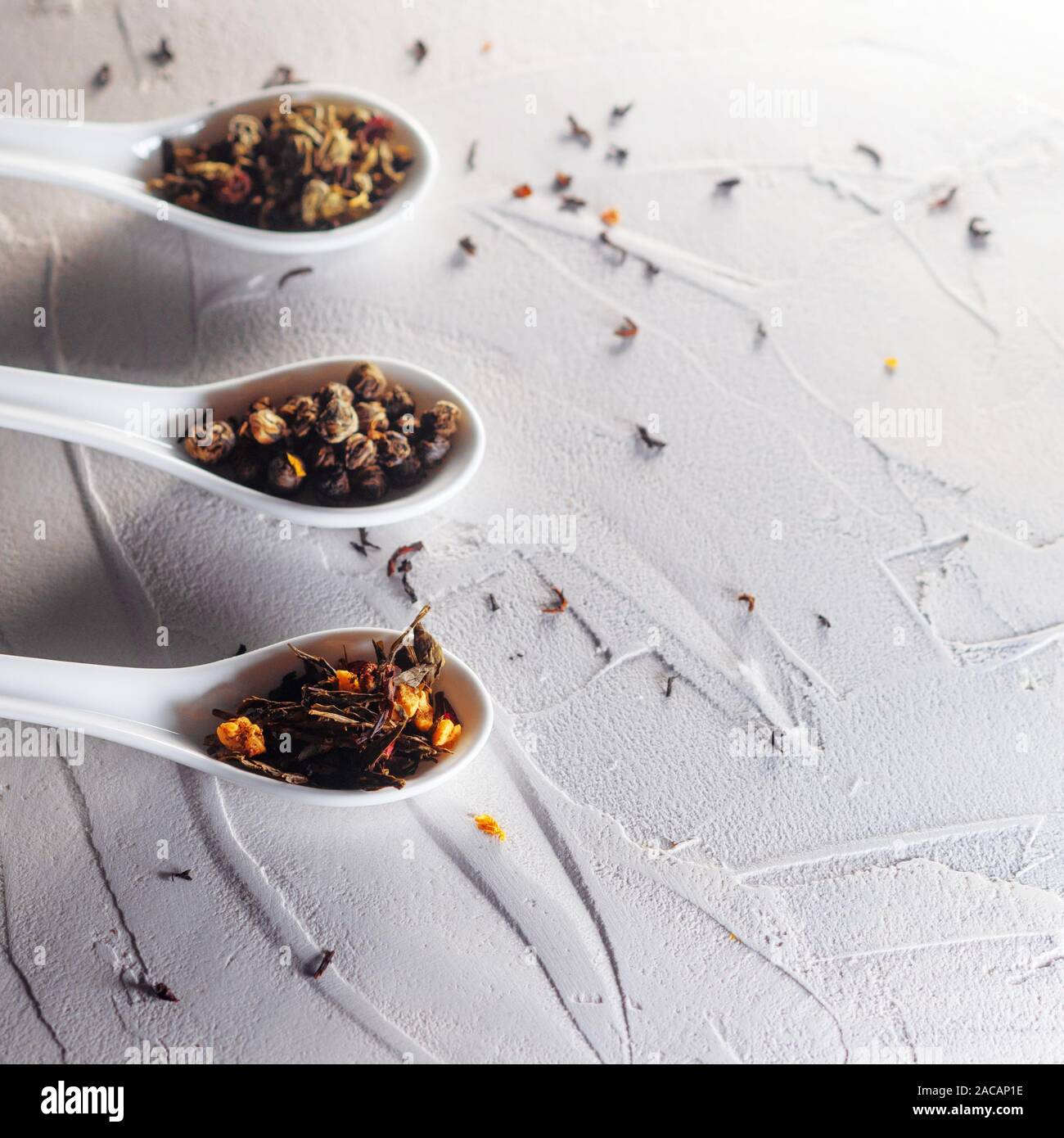 Different varieties of tea leaves in white measuring spoons on a white ...