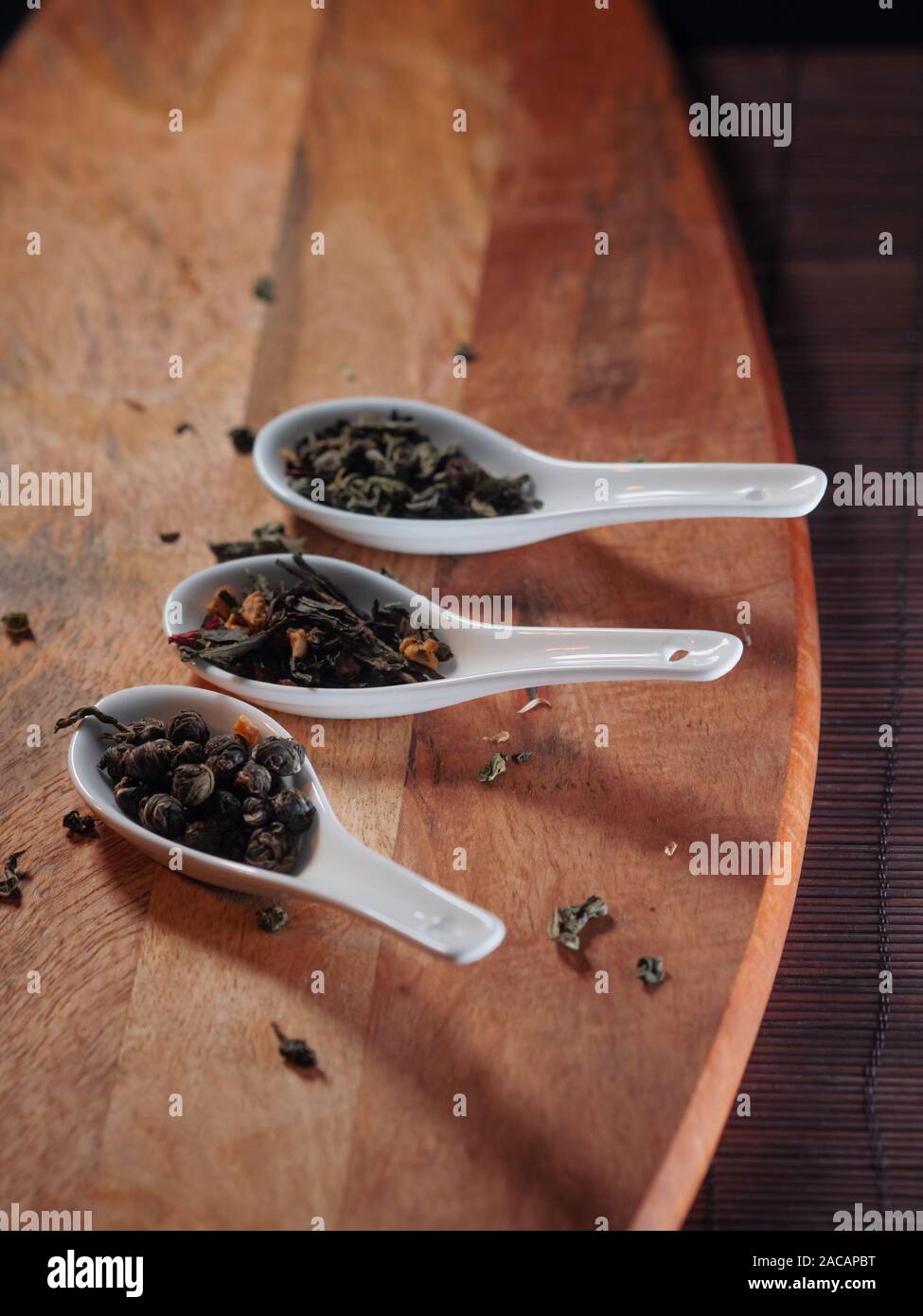 Different varieties of tea leaves in white measuring spoons on a wooden ...