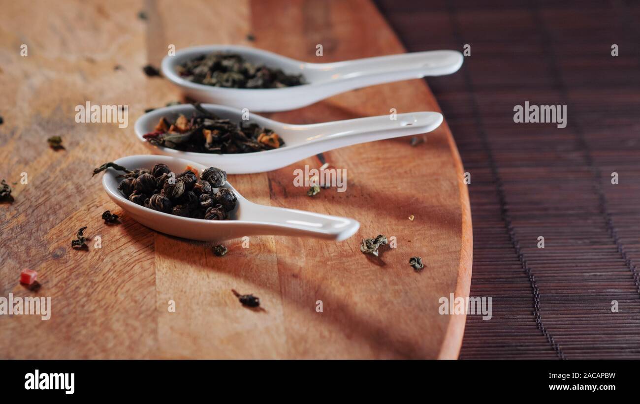 Different varieties of tea leaves in white measuring spoons on a wooden ...