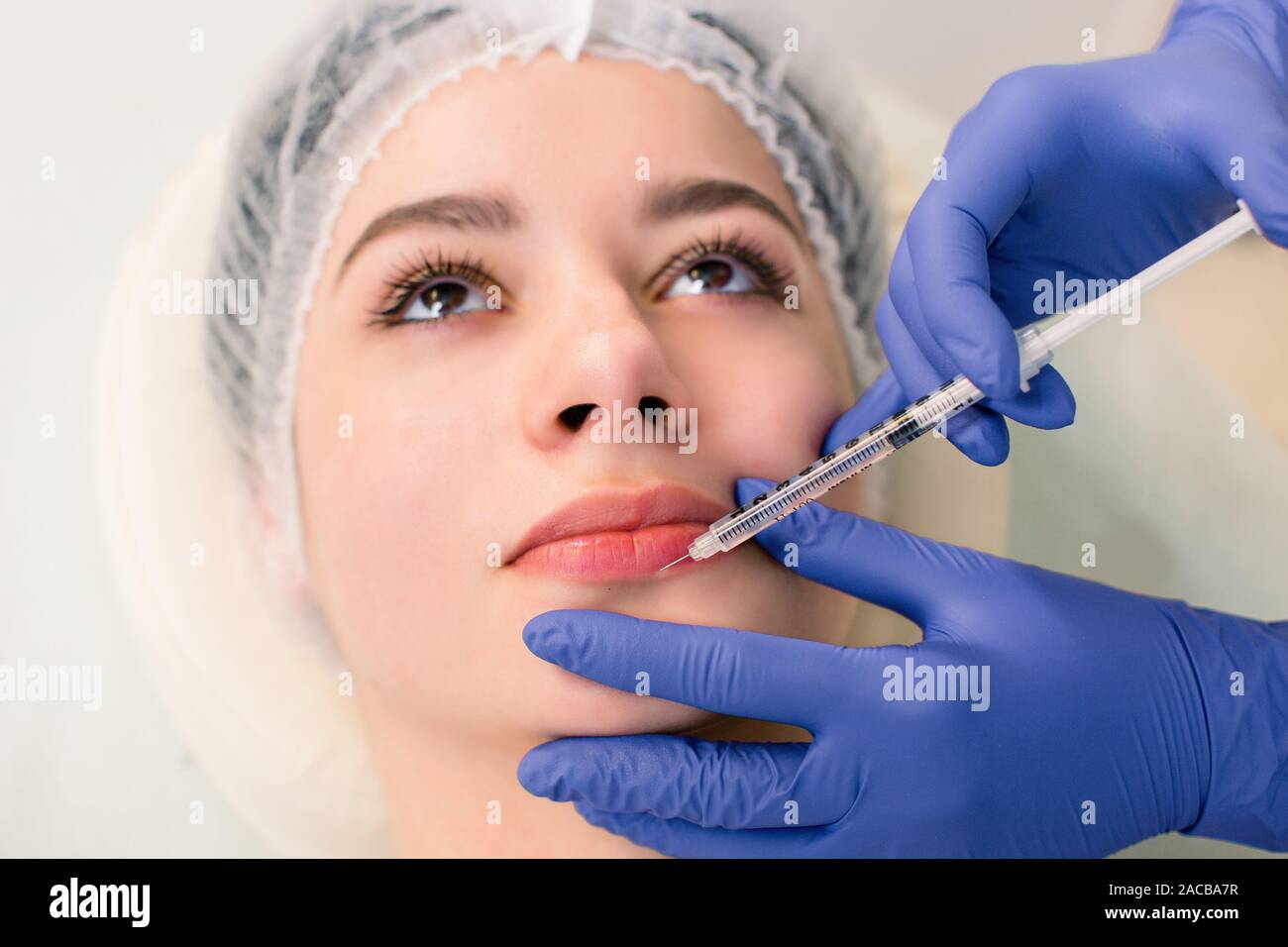 A beautiful woman receives a filler injection on the lips. Young woman receiving a botox ...