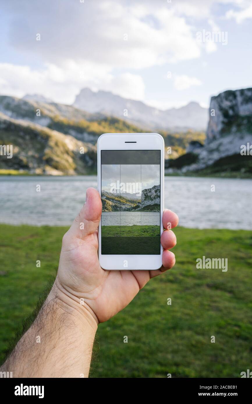 A hand holds a mobile phone making a photo of a mountain landscape with ...