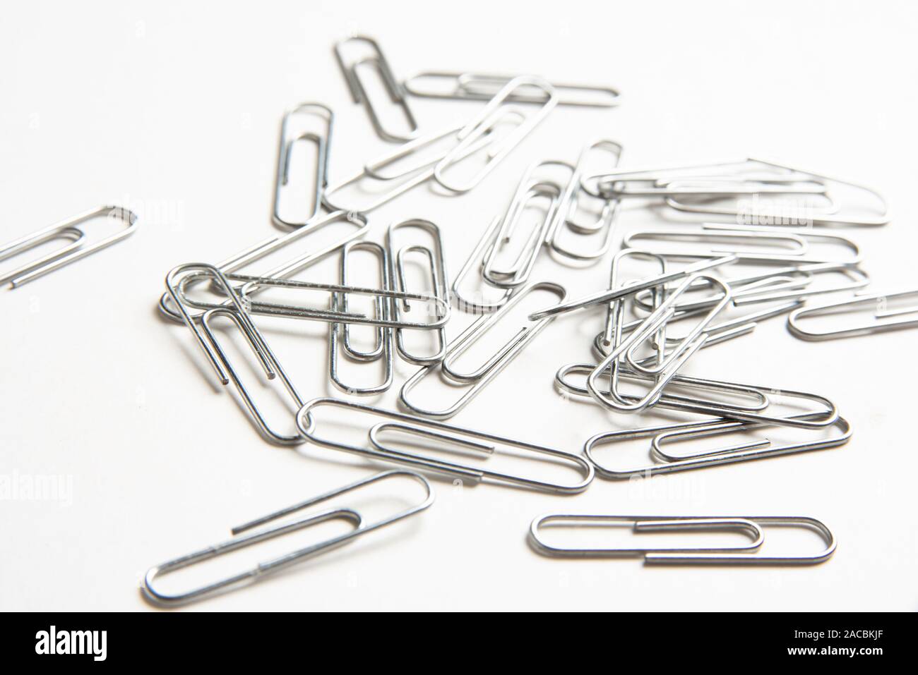 A bunch of silver-color metal paper clips scattered on a plain white ...