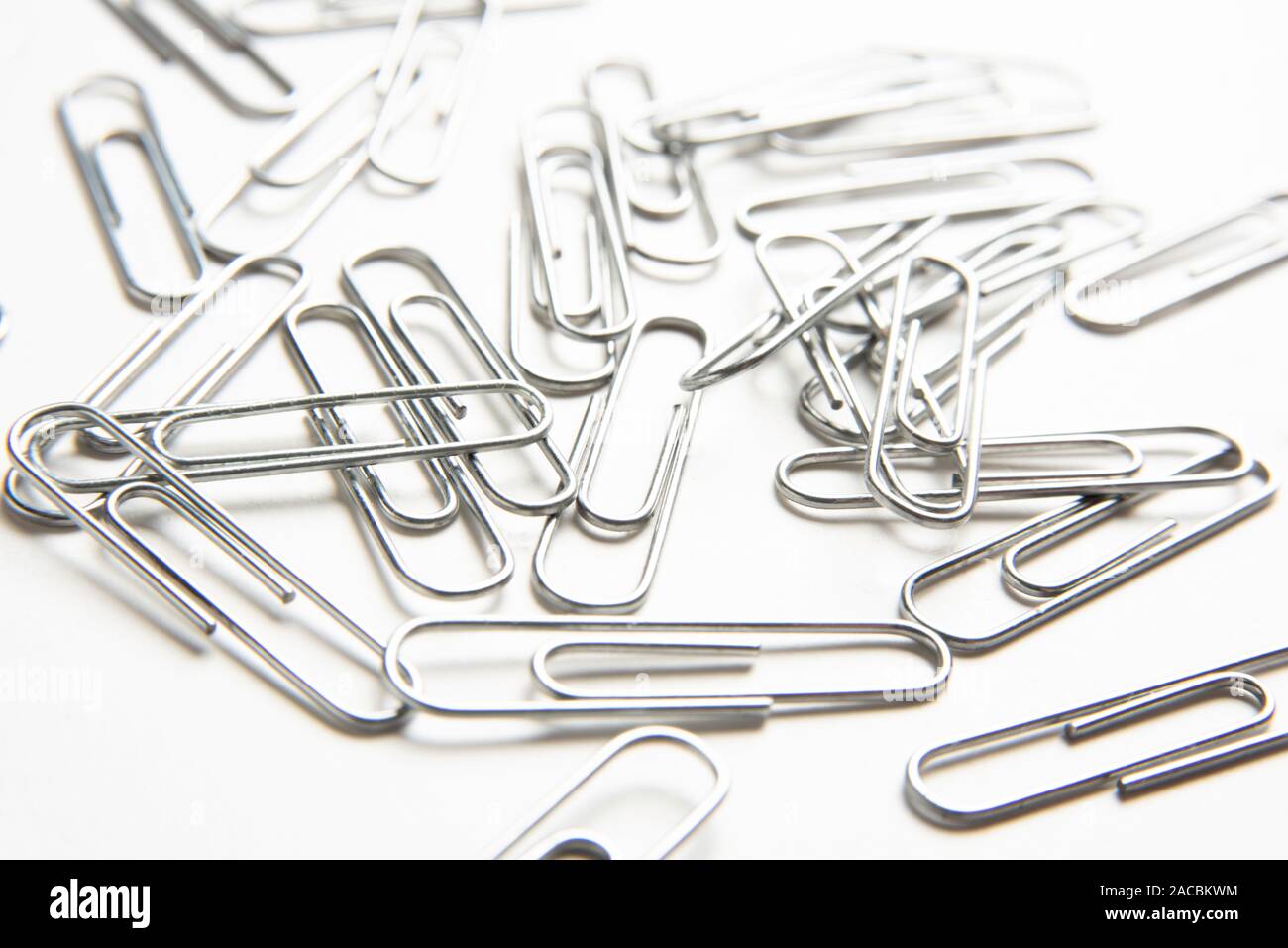 A bunch of silver-color metal paper clips scattered on a plain white ...