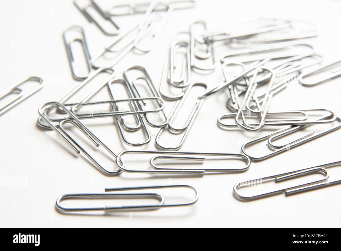 A bunch of silver-color metal paper clips scattered on a plain white ...