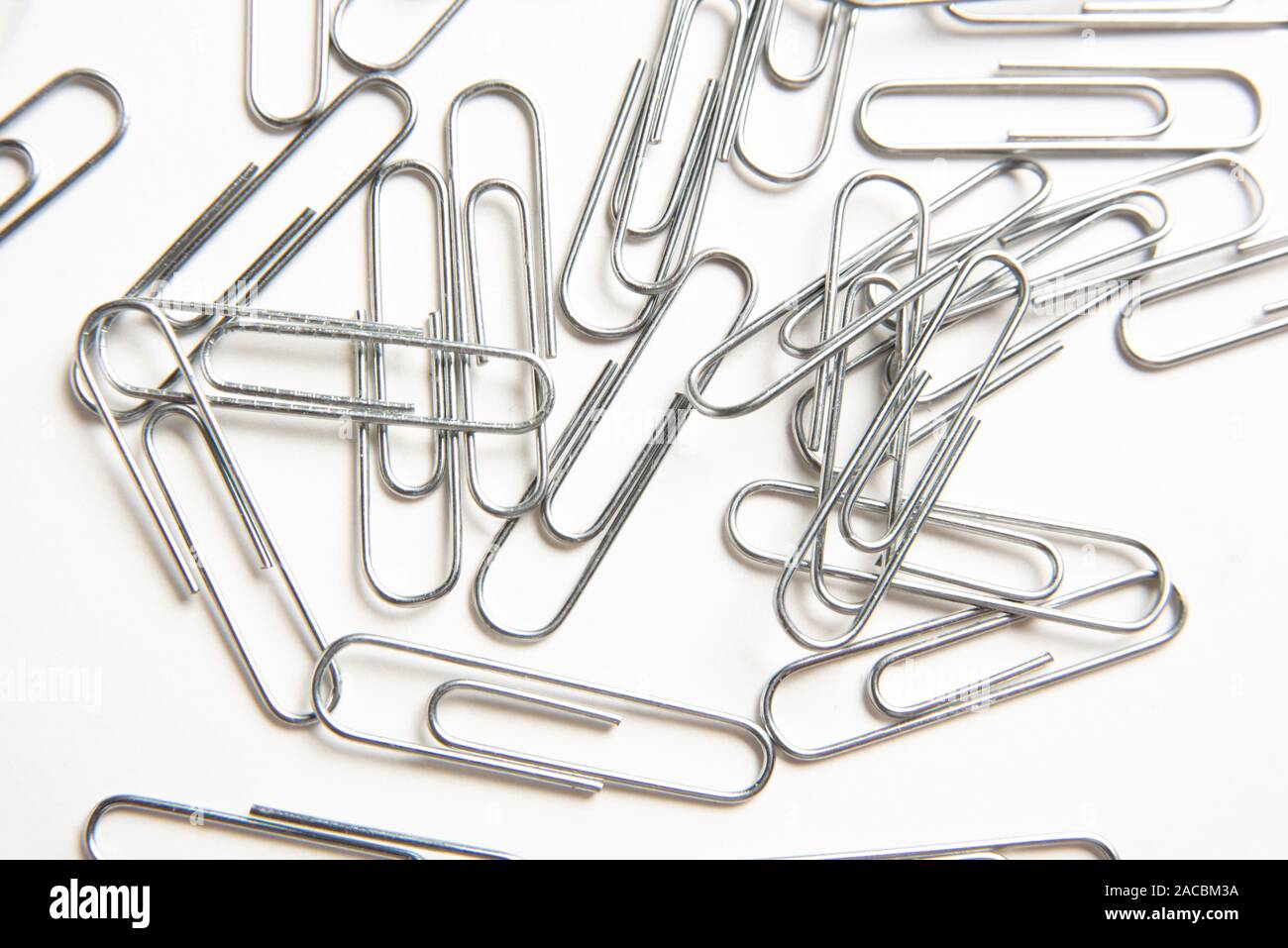 A bunch of silver-color metal paper clips scattered on a plain white ...