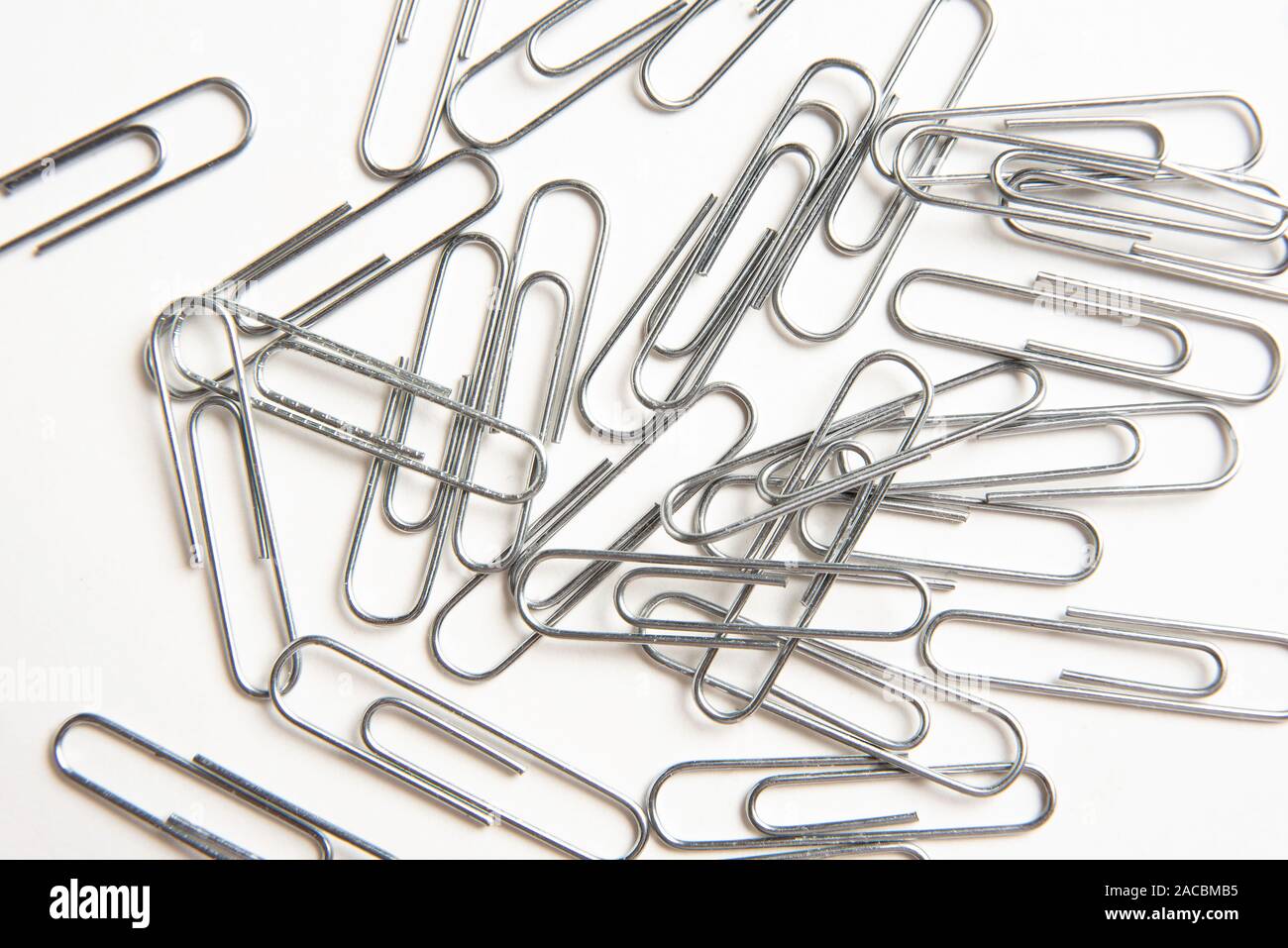 A bunch of silver-color metal paper clips scattered on a plain white ...