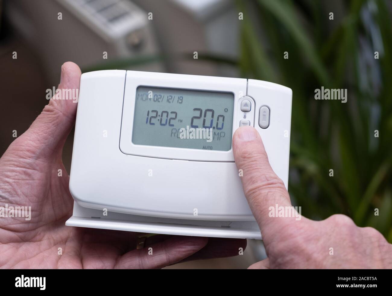 Hand holding central heating controller with modern radiator panel in ...