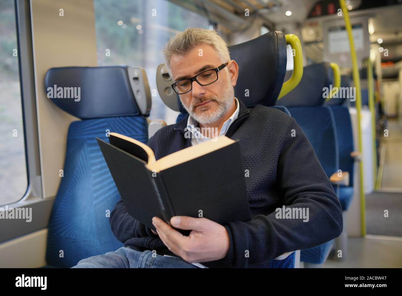 Mature man reading book while traveling on a train Stock Photo - Alamy