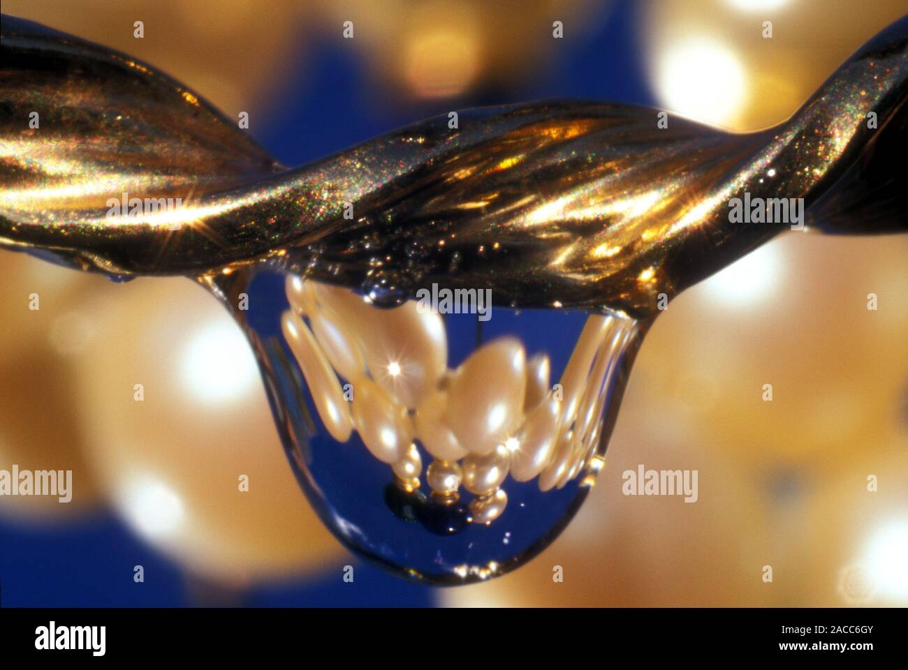 Water droplet on a twist of gold jewellery. The droplet acts as a ...