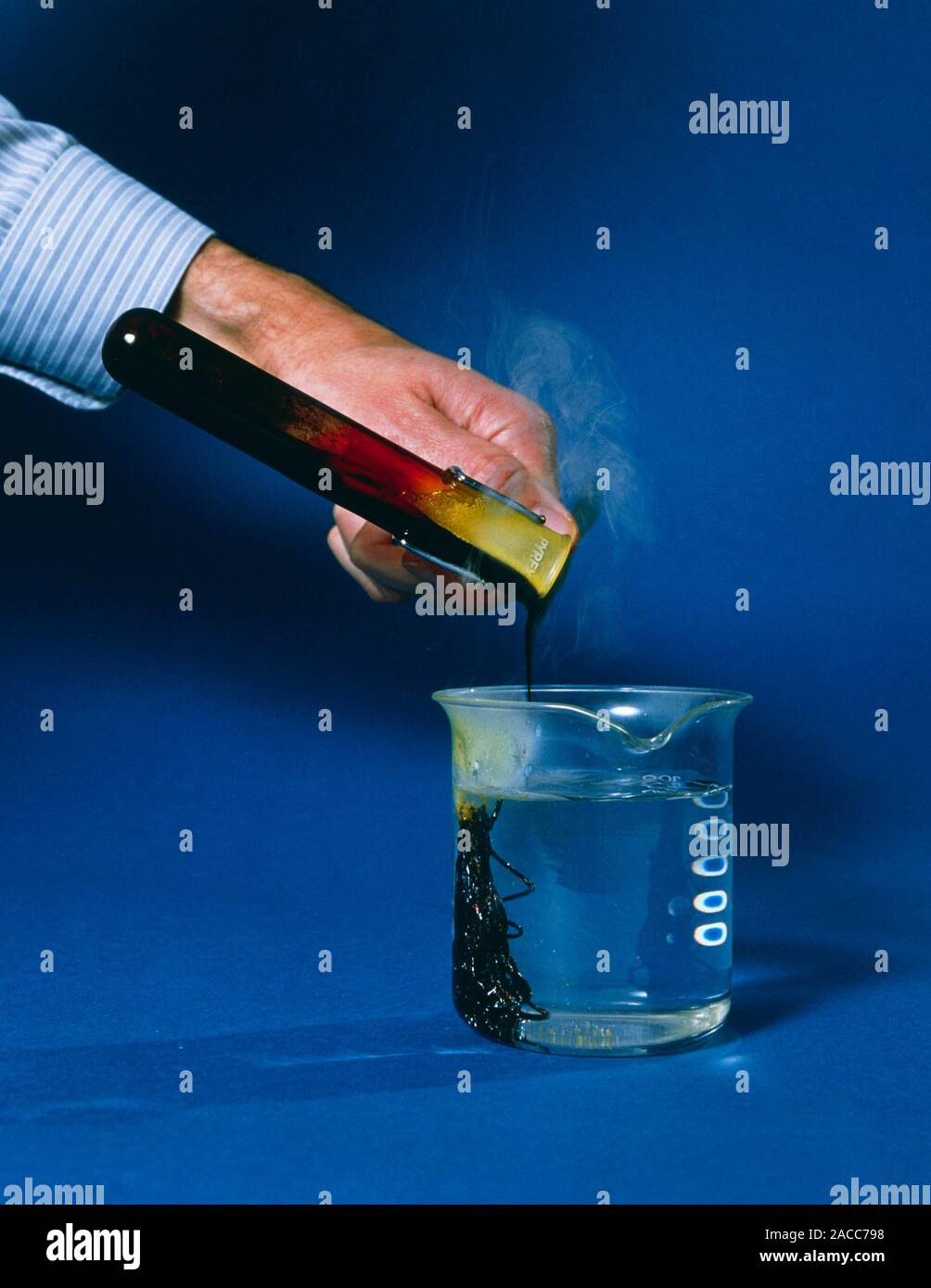 Plastic sulphur. Hand pouring molten sulphur into a beaker of cold ...