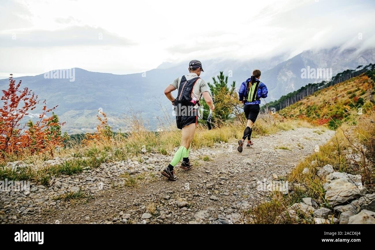 back two men runner with backpacks run mountain trail fall Stock Photo ...