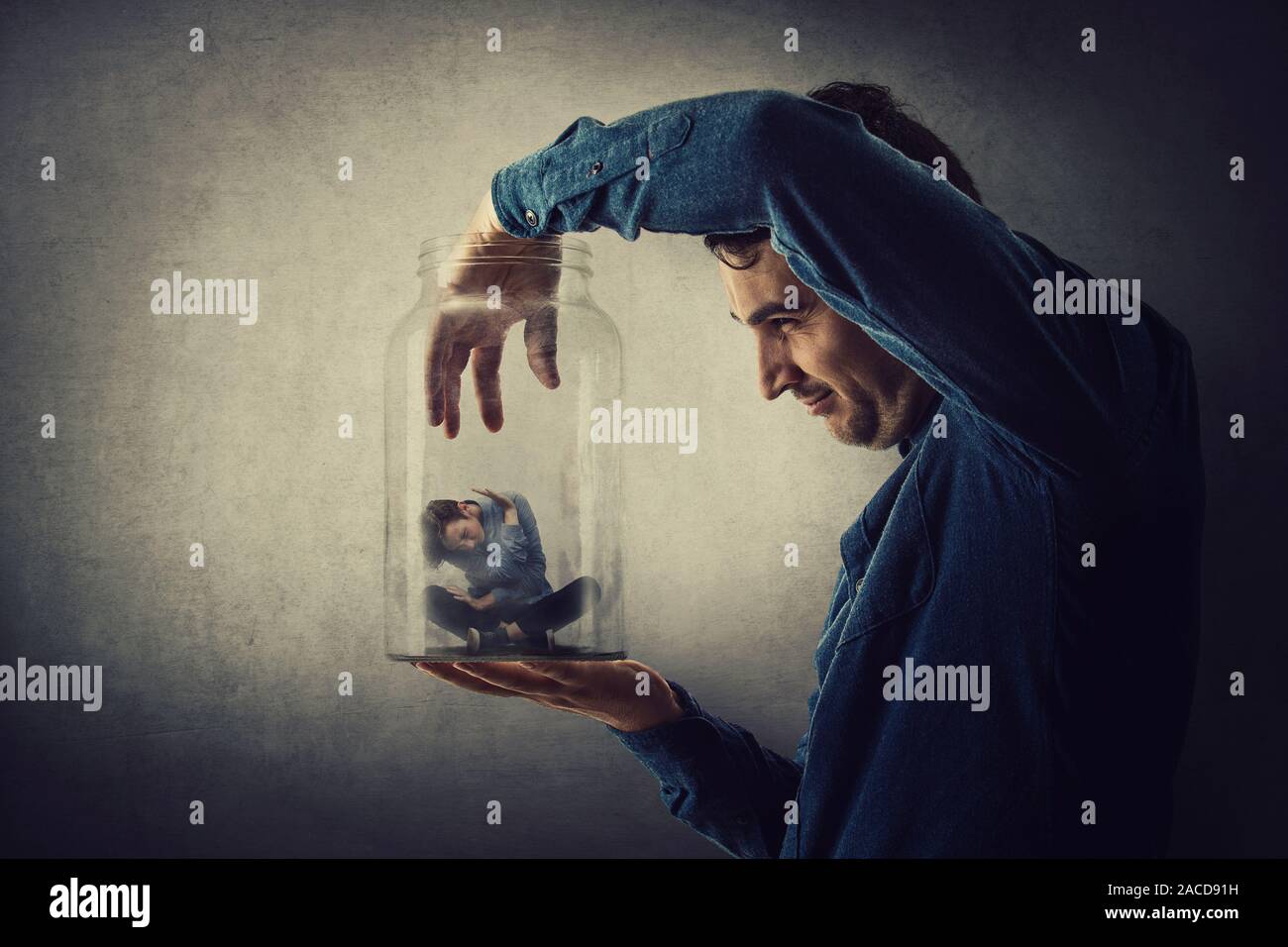 Conceptual scene, scared tiny boy trapped inside a glass jar held in ...