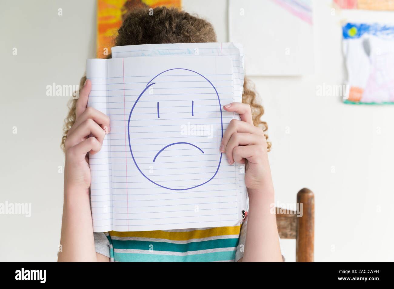 Girl holding note pad with drawing of sad face Stock Photo - Alamy