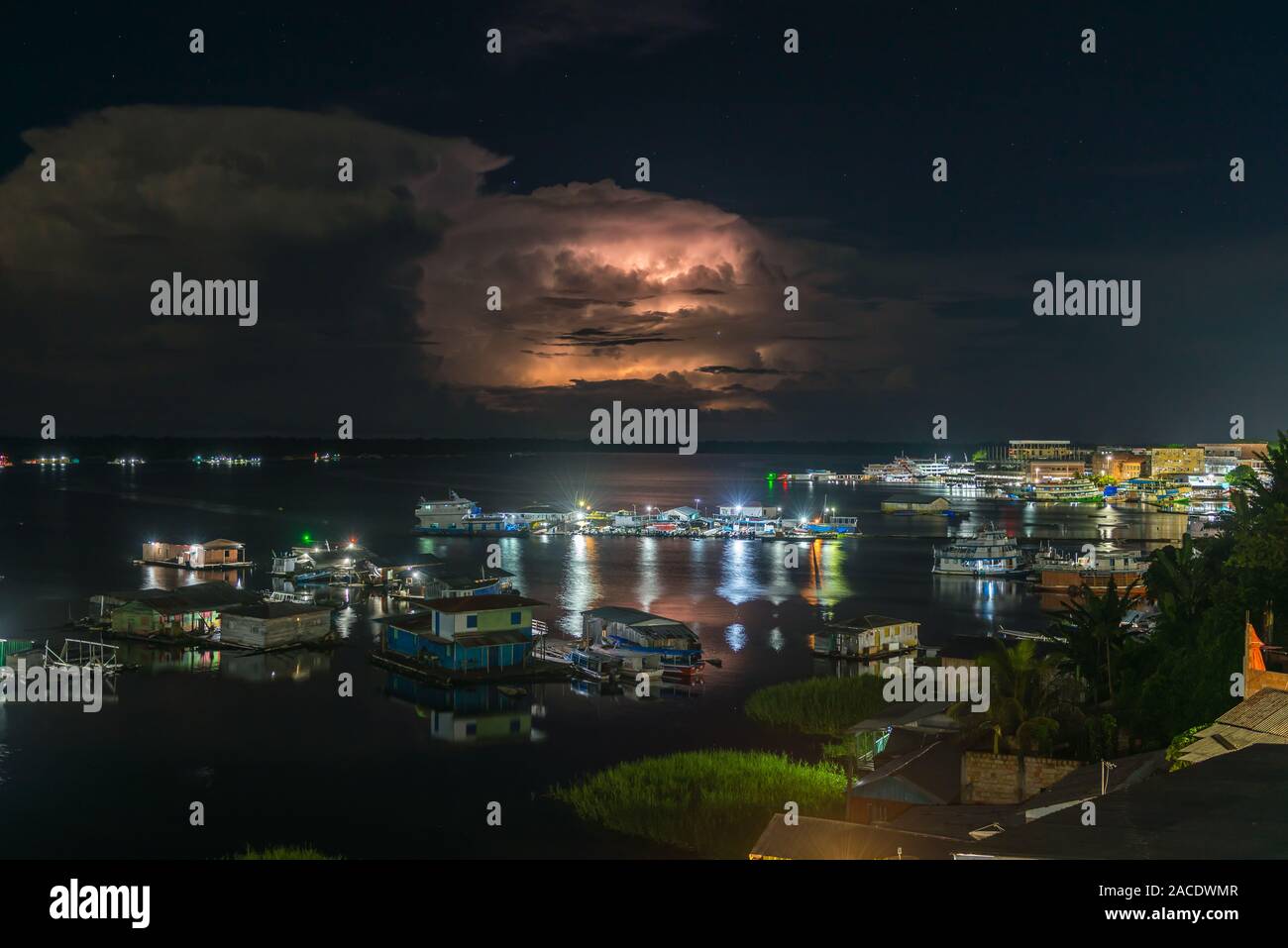 Lightning behind clouds at night, vivid town of Tefé on Lake Tefé ...