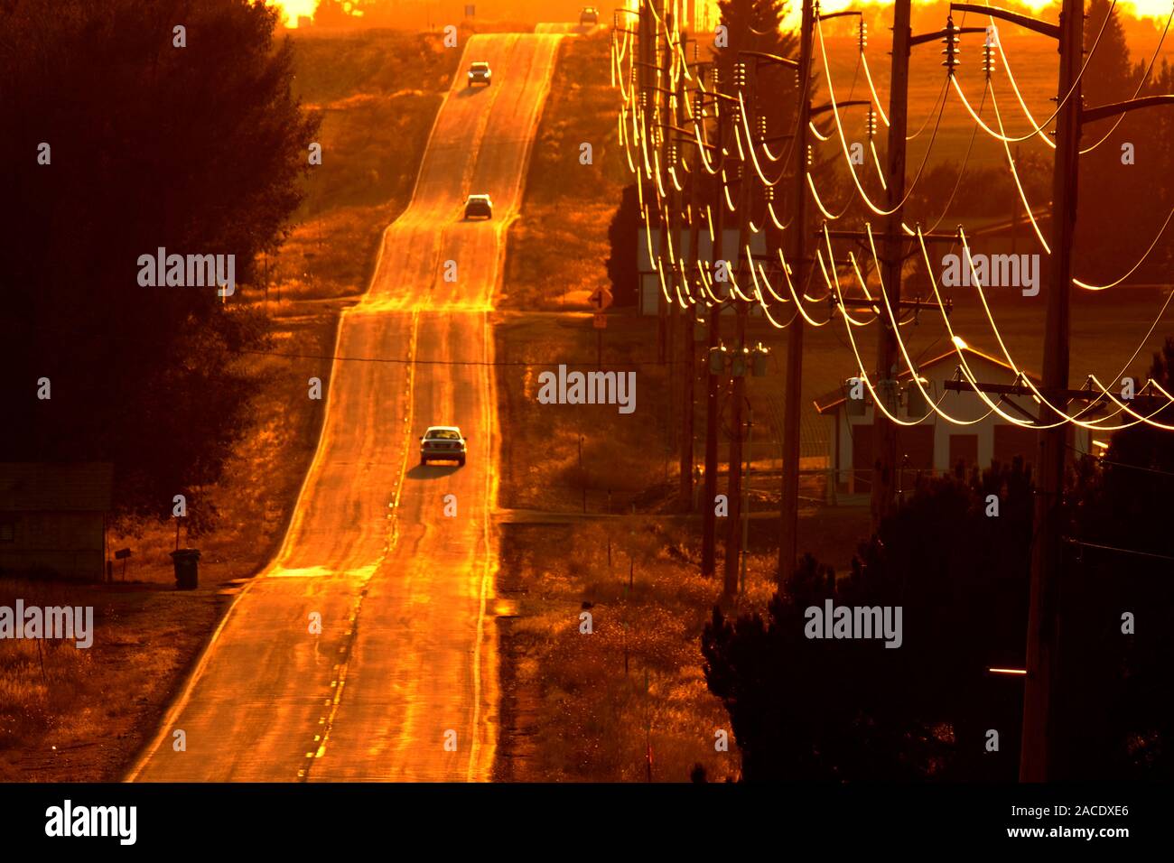 Cars driving on old country road at sunset of sunrise power lines Stock ...