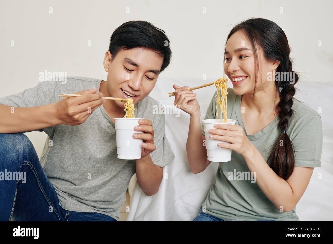 Happy young Vietnamese couple eating tasty ramen from plastic cups ...