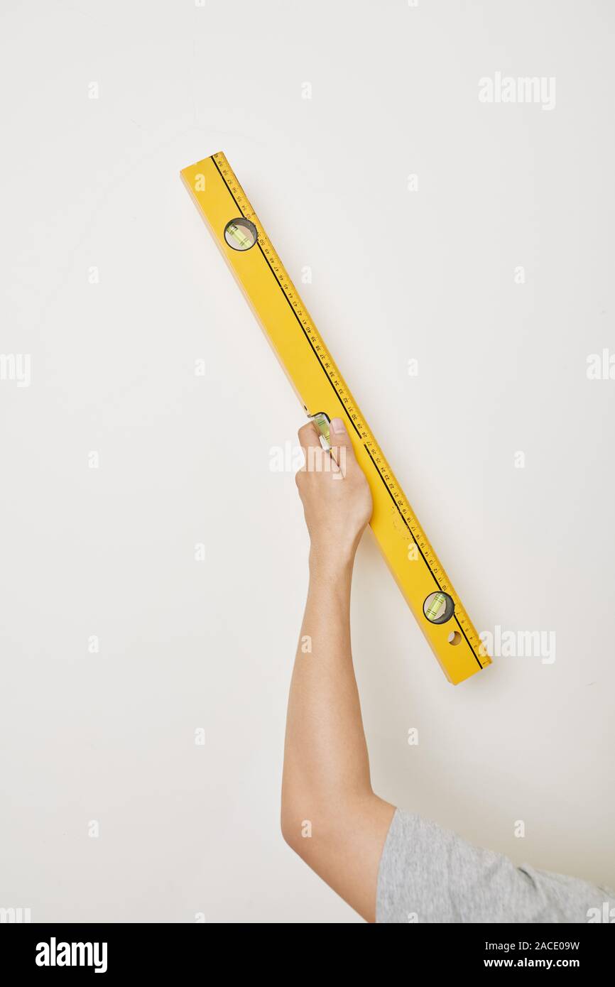 Hand of repairman holding spirit level against white wall in new ...
