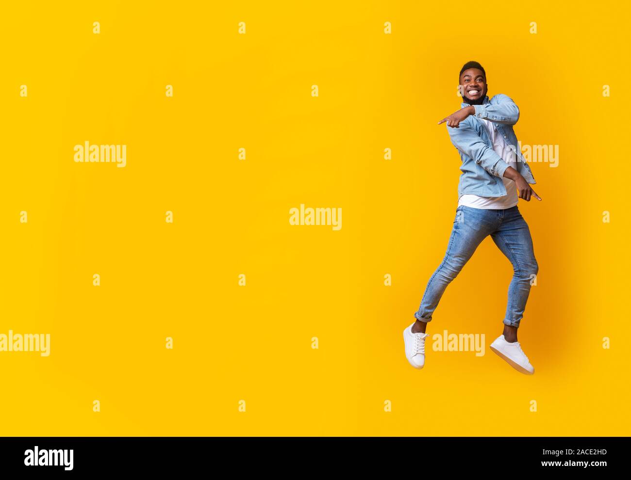 Funny jumping black guy pointing at copy space on yellow background ...