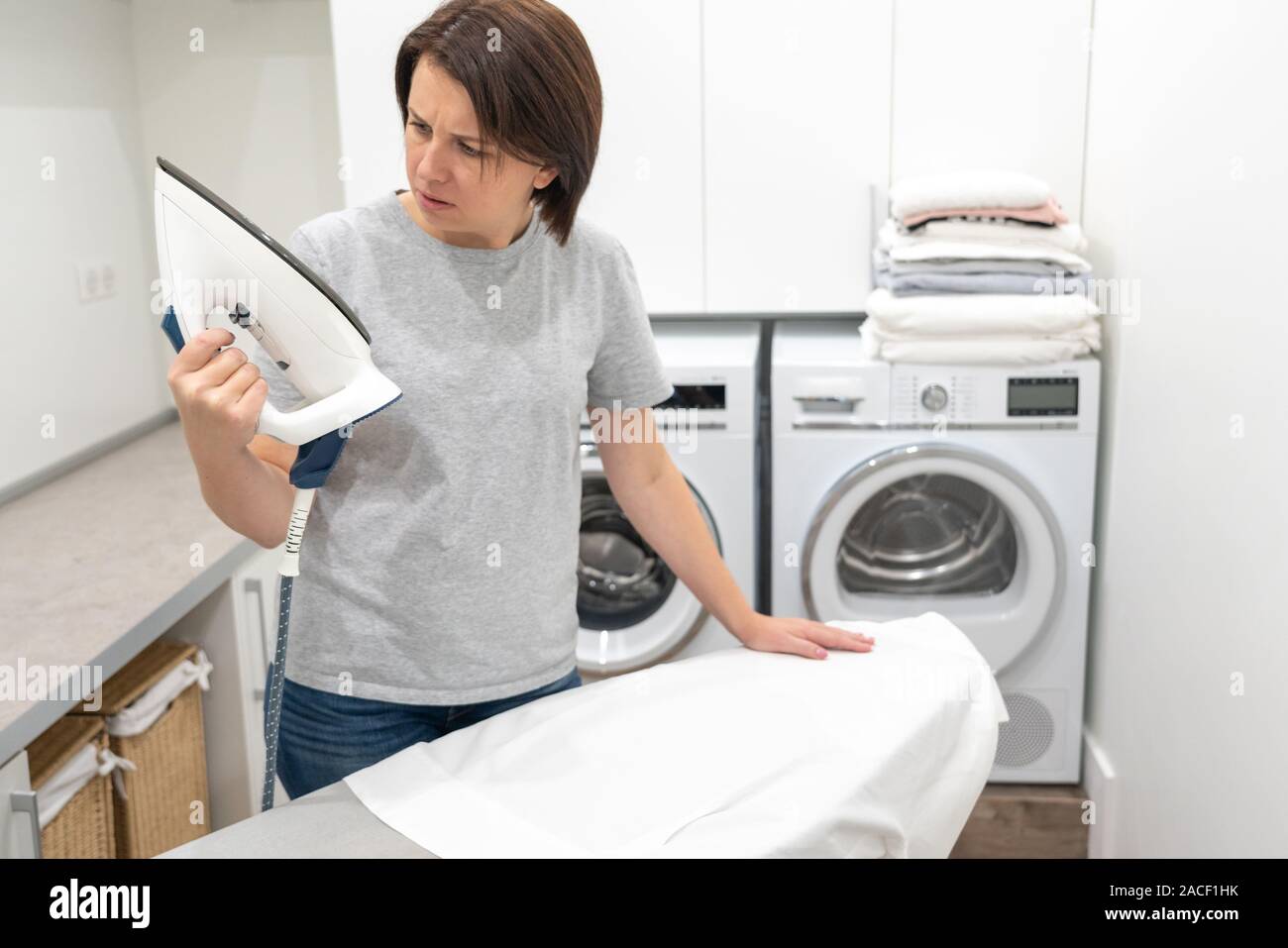 Woman ironing white shirt on board in laundry room with washing machine ...