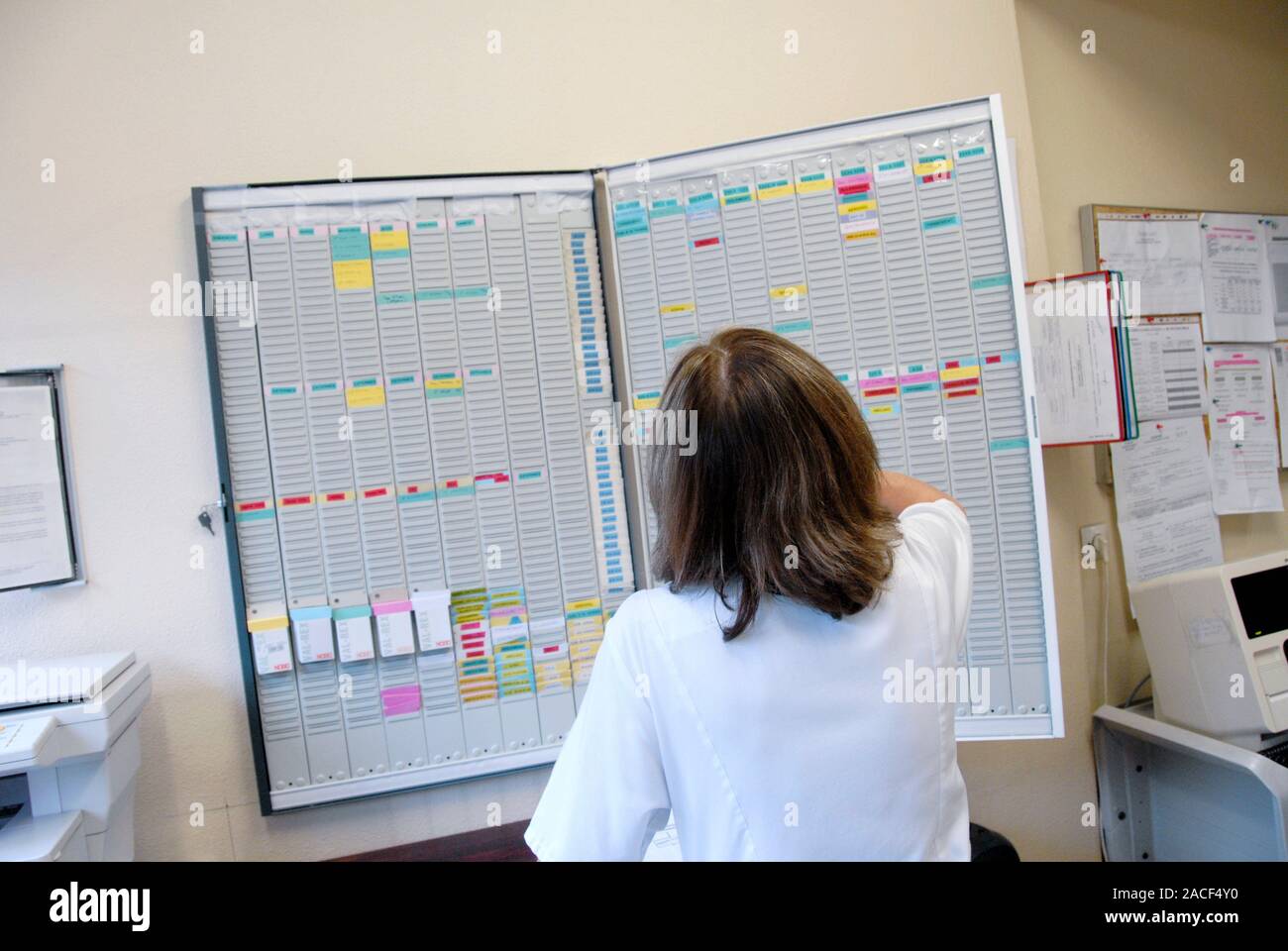 Nurse and hospital noticeboard. Nurse at her workstation examining a ...