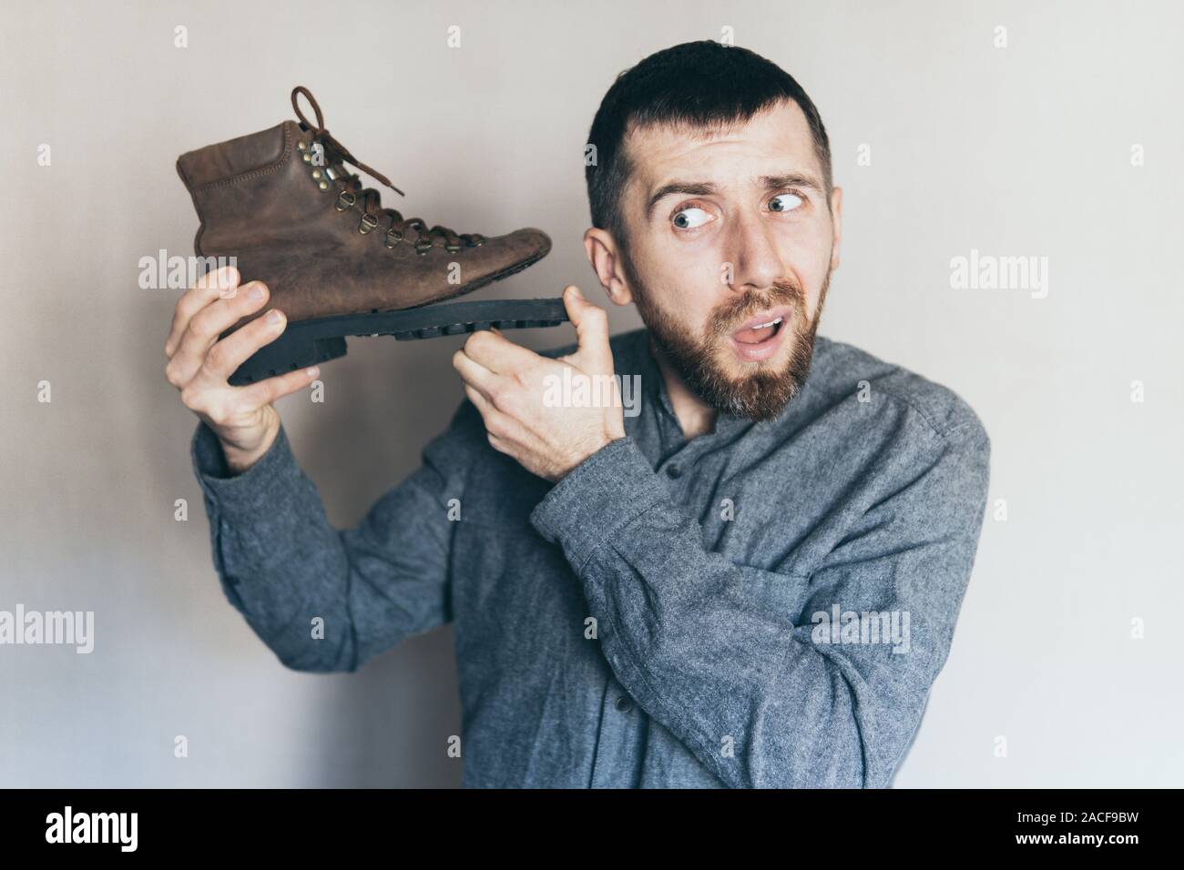 Young bearded Caucasian man holds old leather boot with torn sole ...