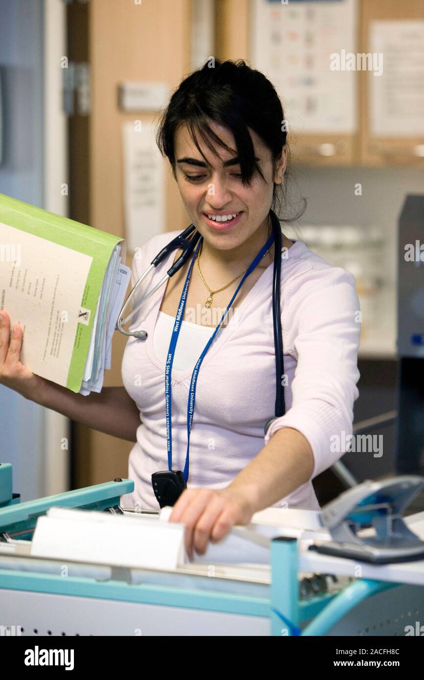 Hospital doctor smiling whilst looking through patient notes ...