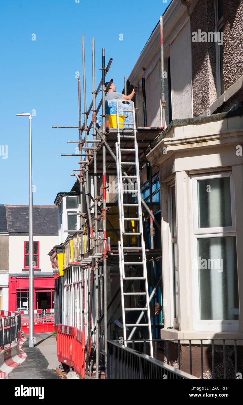Workman applying plaster to a house wall whilst standing on scaffolding ...