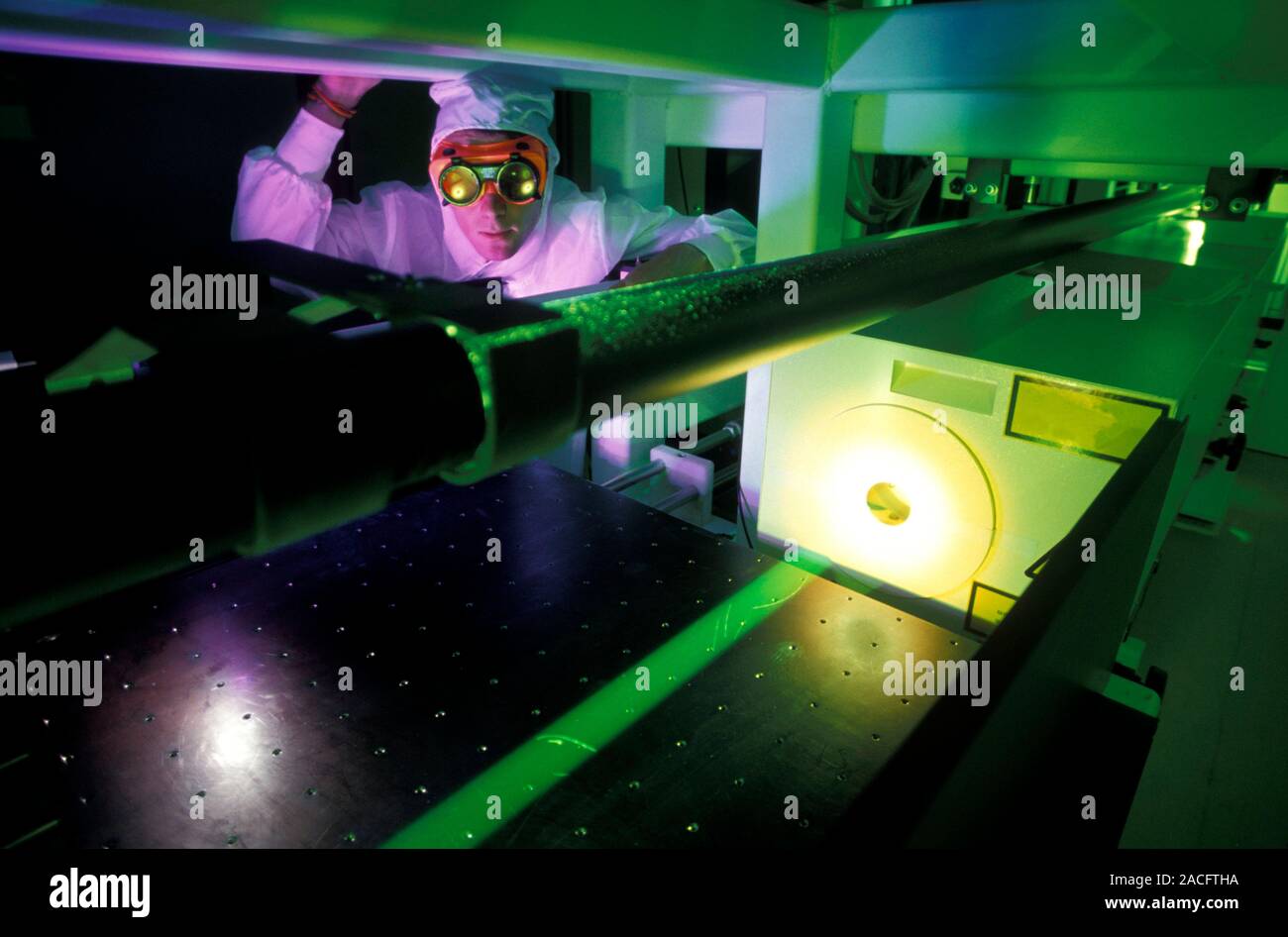 Laser research. Laser equipment being observed by a researcher who is ...
