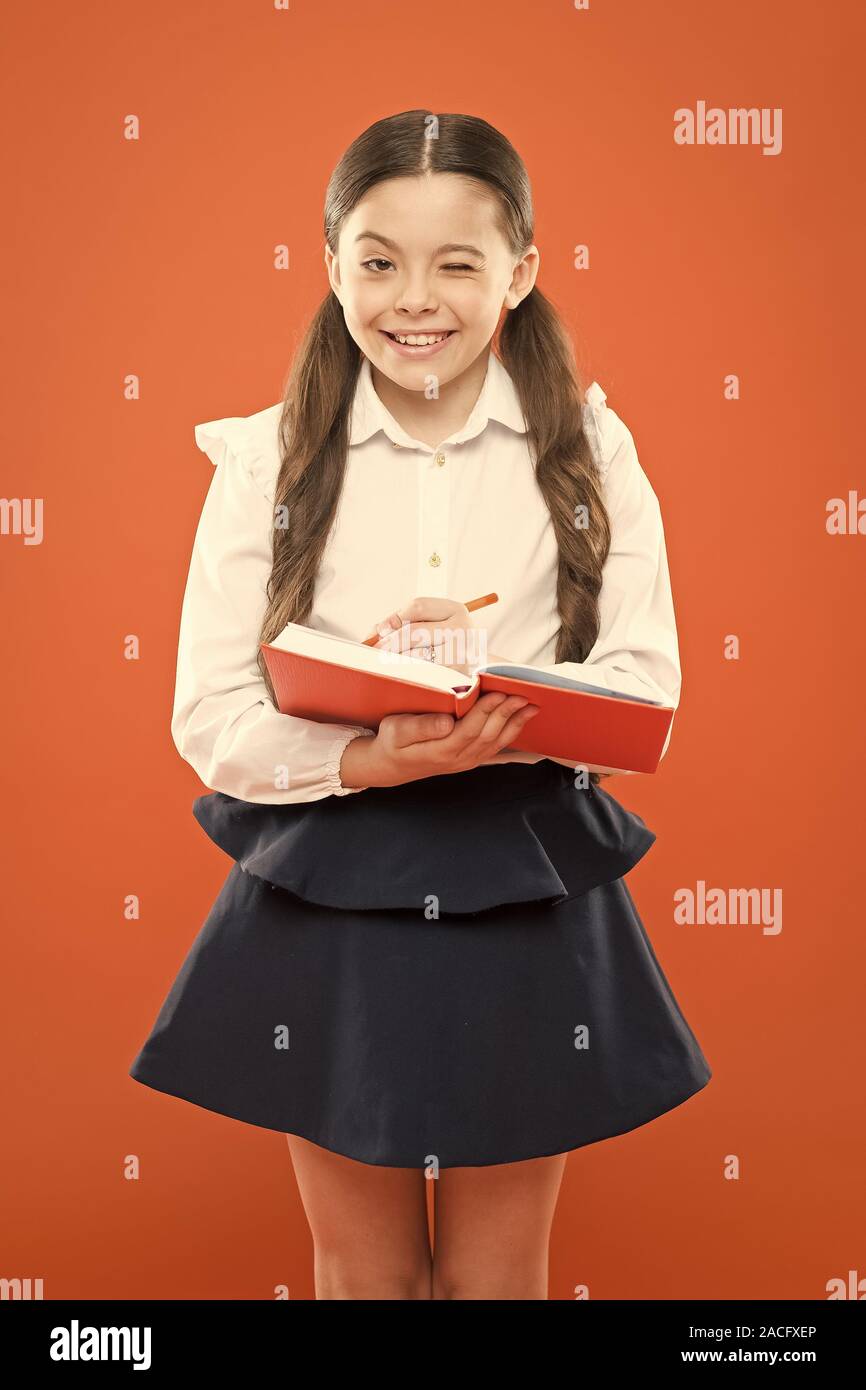 schoolgirl writing notes on orange background. small girl in school ...