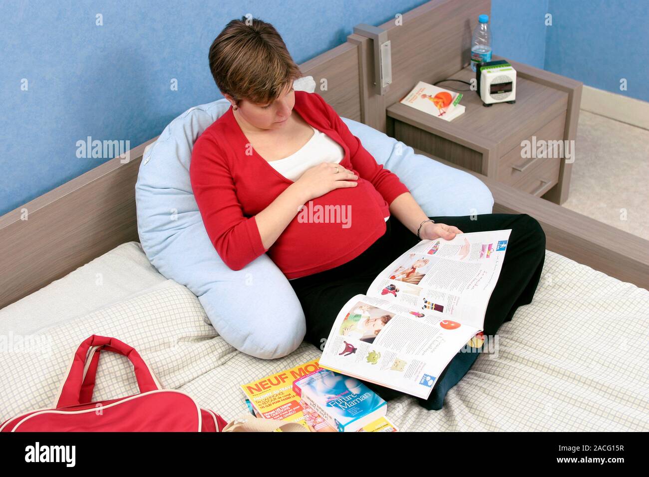 Pregnant woman reading a maternity book on a bed, with one hand holding ...