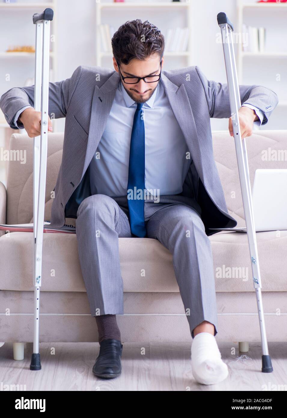 The businessman with crutches and broken leg at home working Stock ...