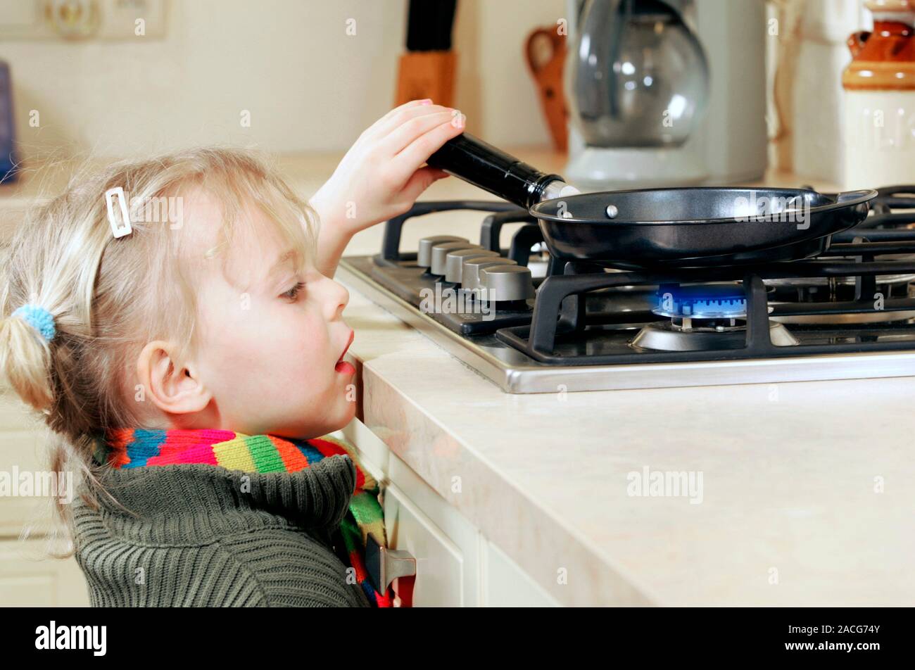 Home safety. Young girl about to pull a hot frying-pan off a lit oven ...