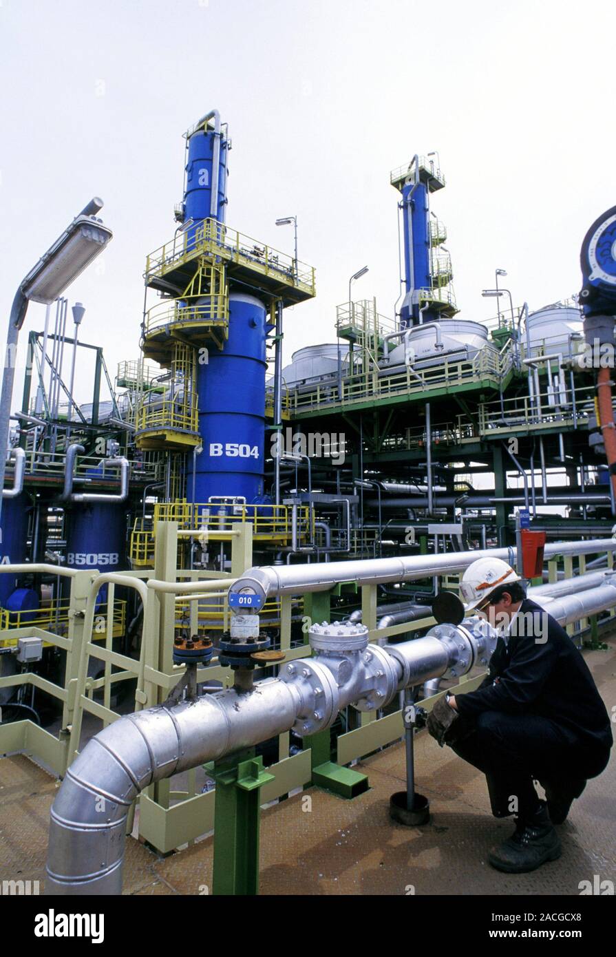 Oil refinery. Technician checking pipework at a petroleum plant ...