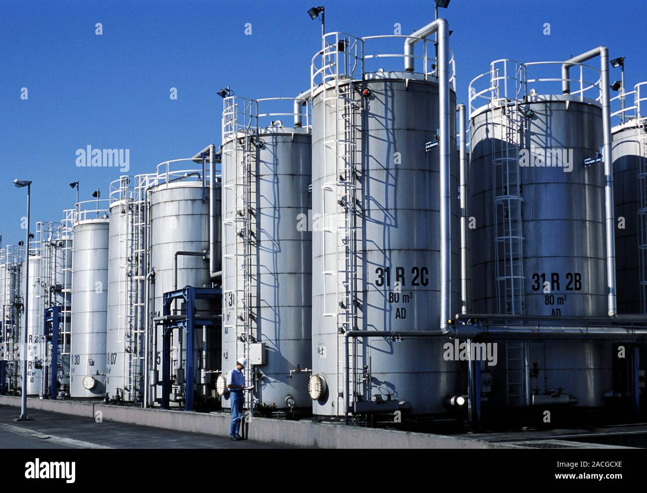 Oil refinery. Technician monitoring storage tanks containing petroleum ...