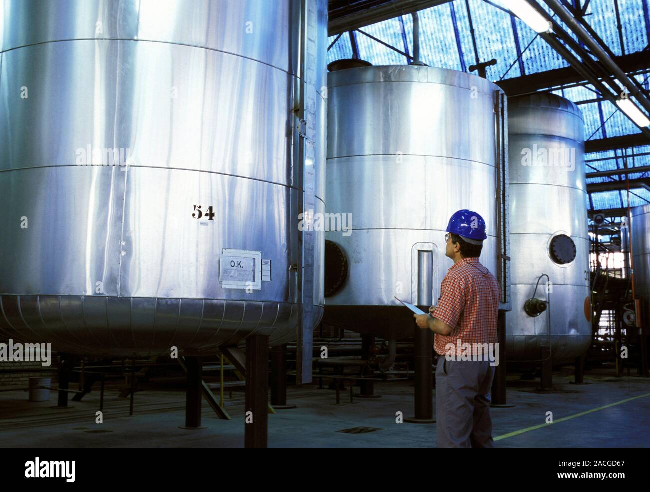Oil refinery. Technician checking storage tanks at a petroleum plant ...