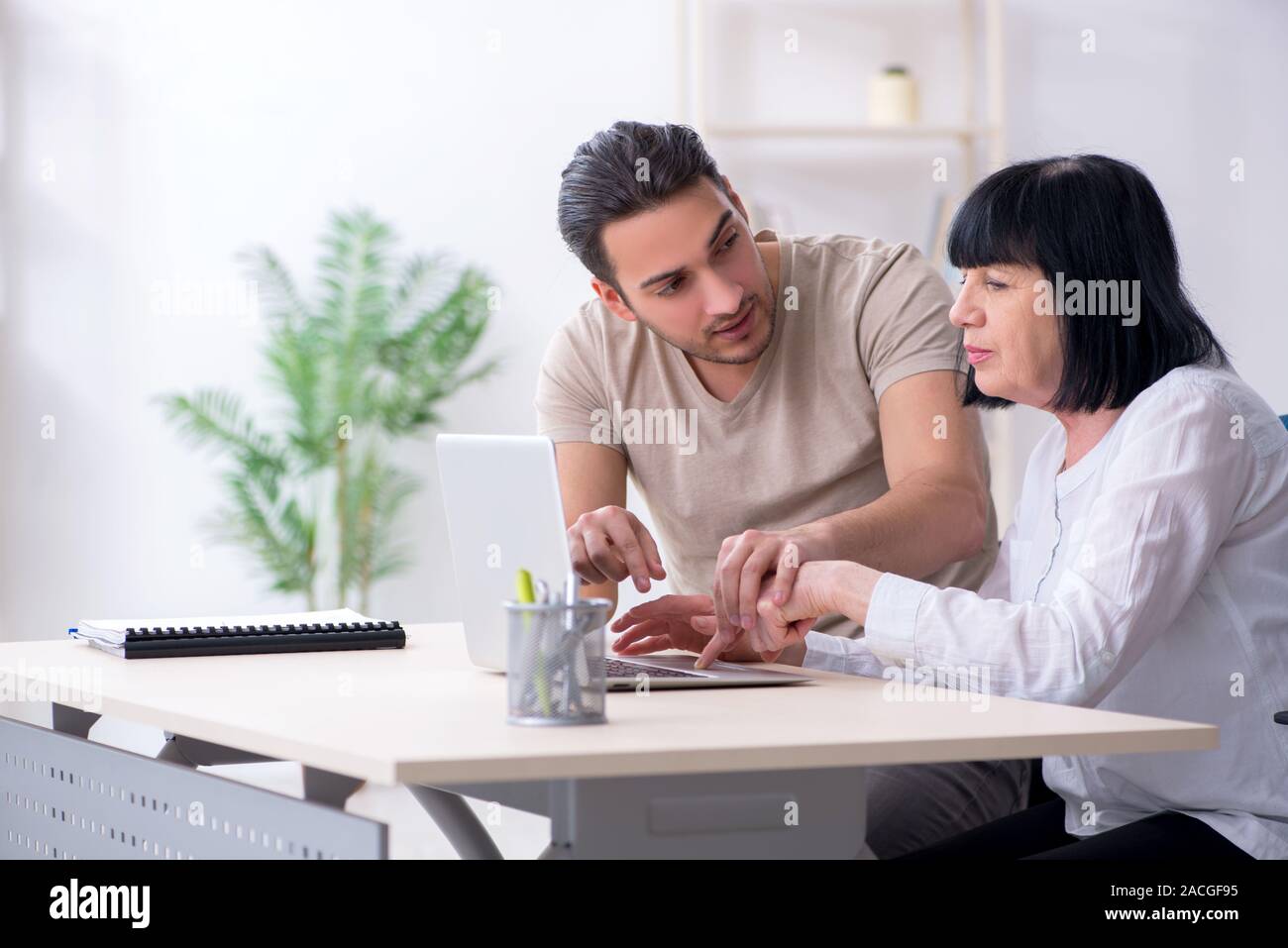 Young male employee explaining to old female colleague how to use ...