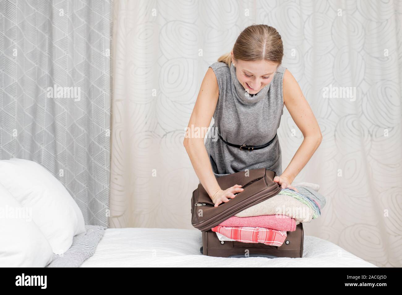 Beautiful woman packing suitcase in bedroom getting ready for road trip ...