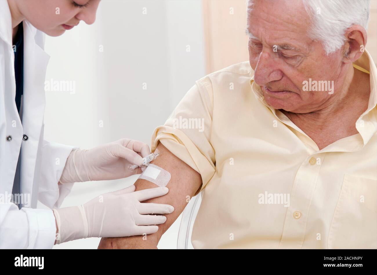 Geriatric care. Nurse putting a plaster on an older man's arm after giving him an injection ...