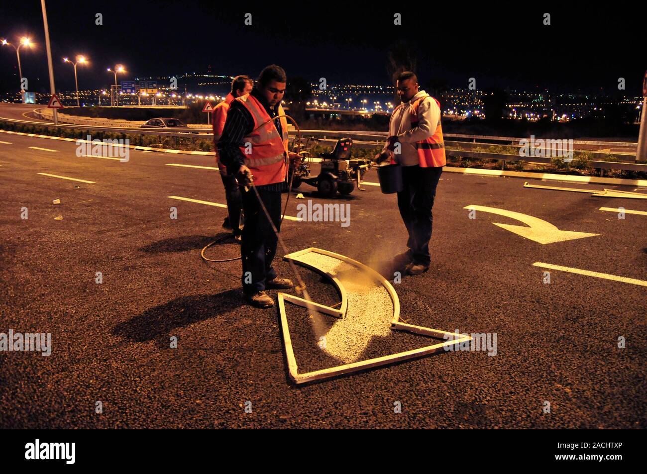 Painting road markings. Workers painting arrows on a road at night ...